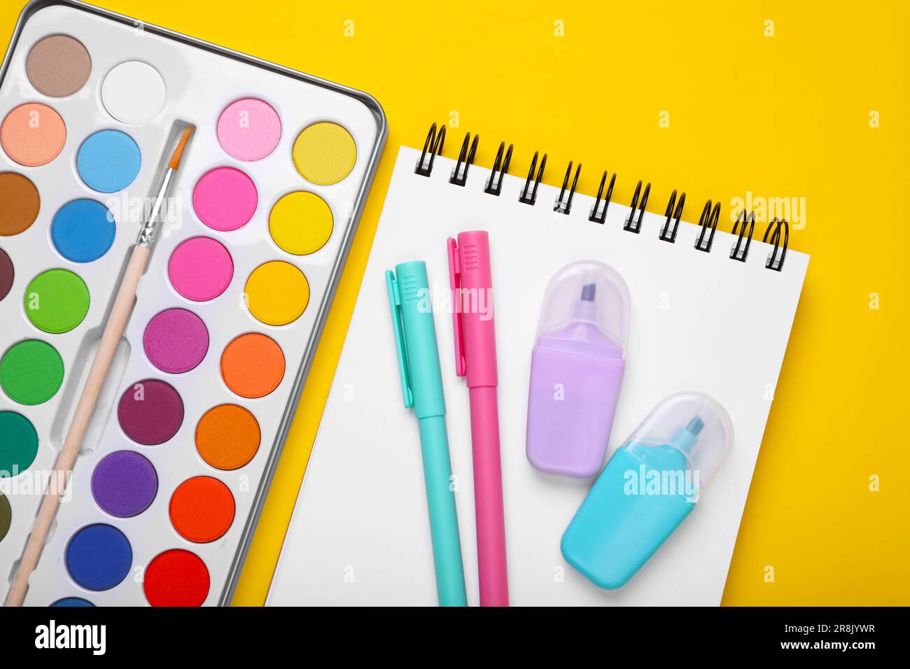 Watercolor palette, notebook and colorful markers on yellow background ...