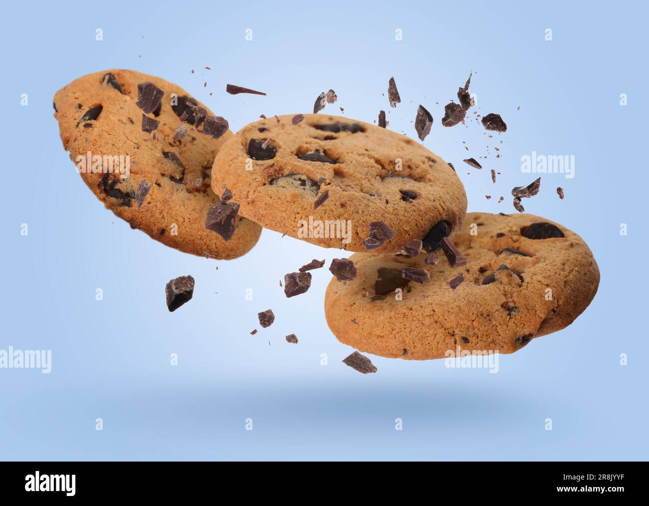 Tasty chocolate chip cookies falling on light blue background Stock ...
