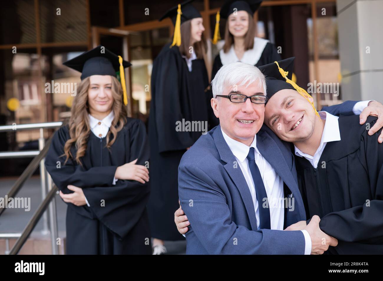 A gray-haired male teacher congratulates students on their graduation ...