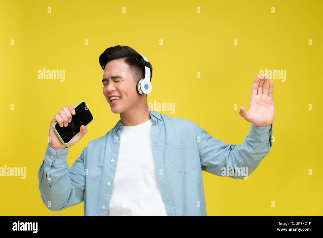 Portrait of overjoyed asian guy singing song and using smart phone as ...