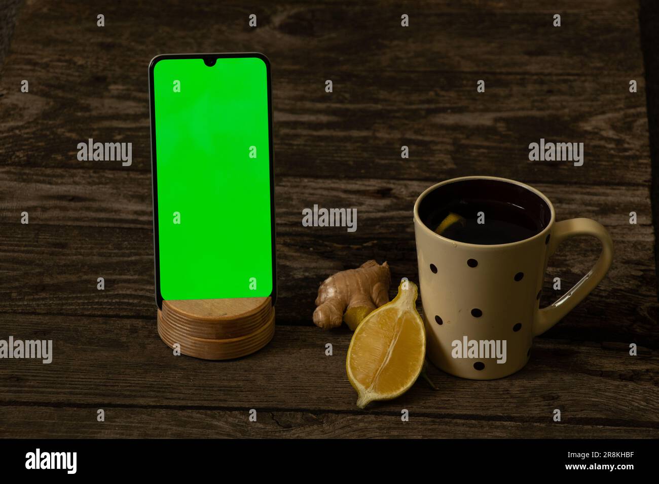 mobile phone with a green screen and a cup of tea with lemon on an ...