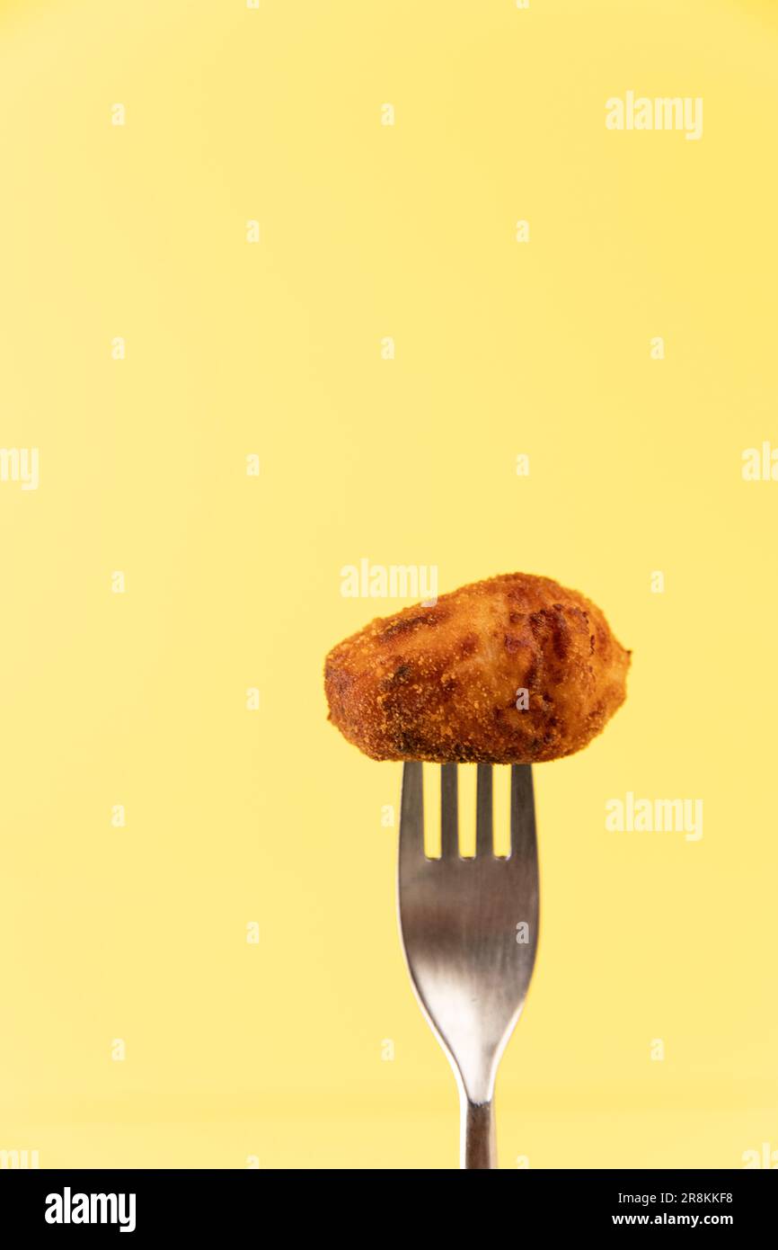Homemade traditional spanish croquette on a fork on yellow background ...