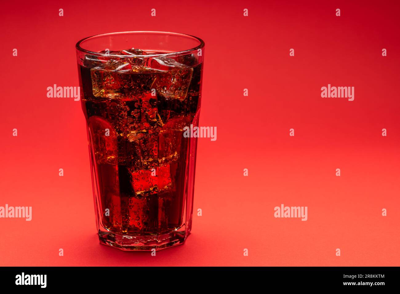 Glass full of ice cubes and a fresh cold cola over red background with ...