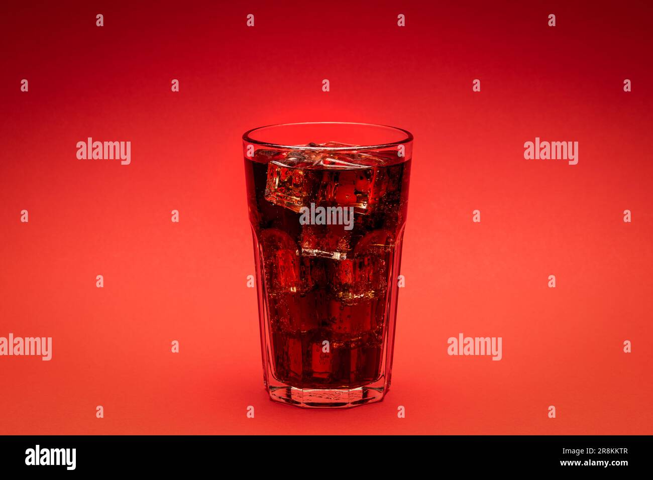 Glass full of ice cubes and a fresh cold cola over red background Stock ...