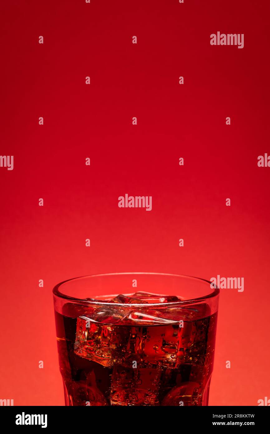 Glass full of ice cubes and a fresh cold cola over red background with ...