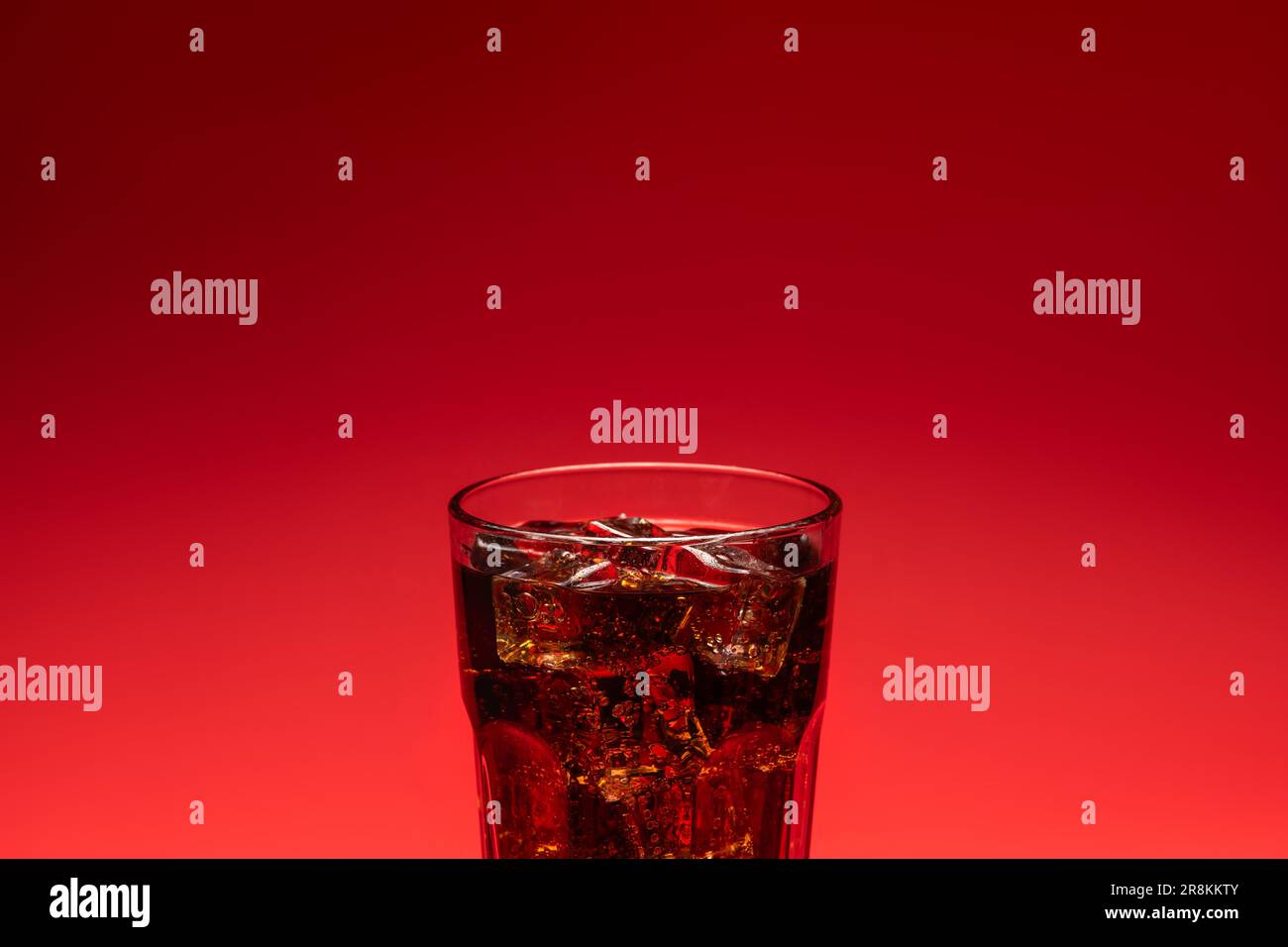 Glass full of ice cubes and a fresh cold cola over red background with ...