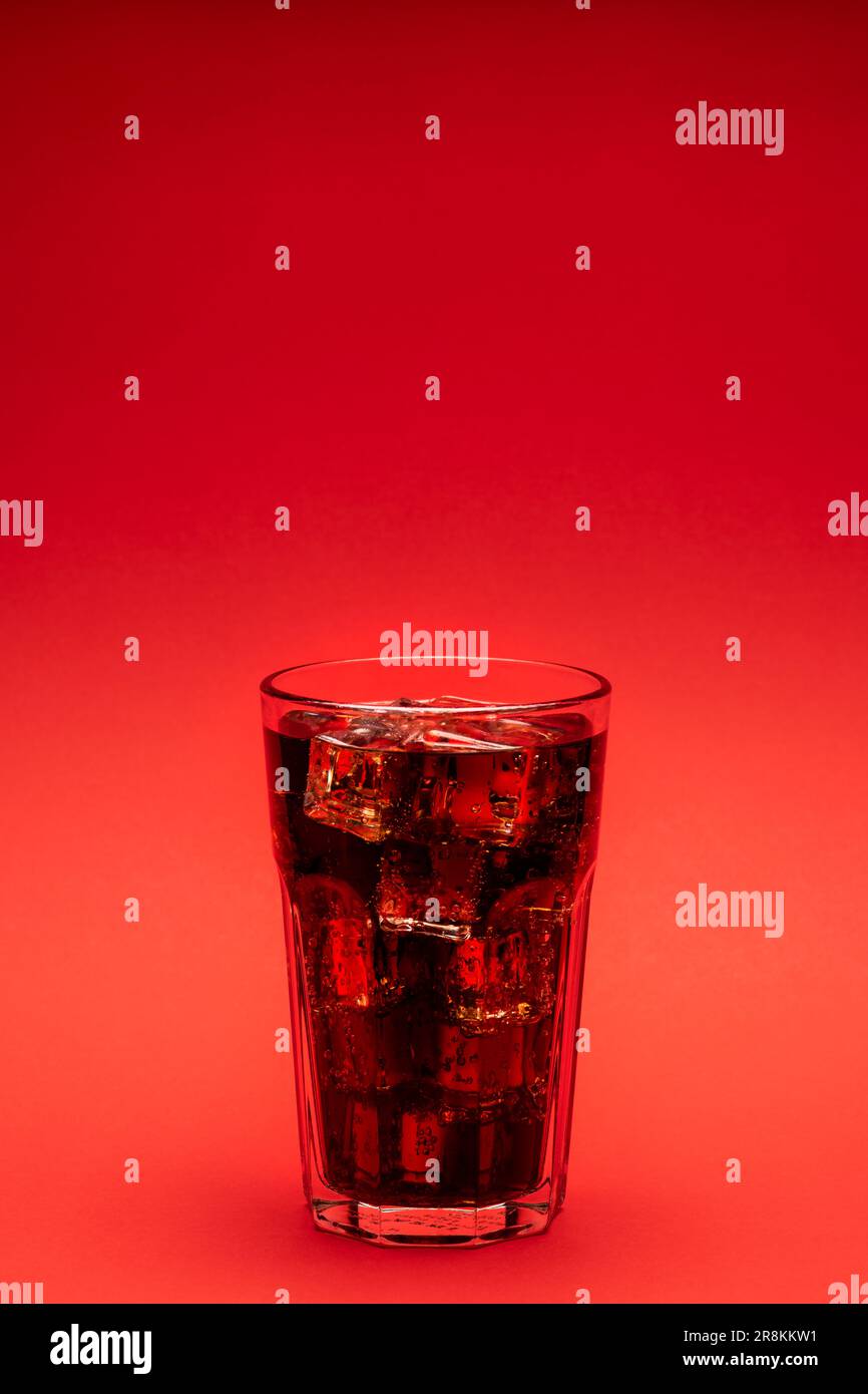 Glass full of ice cubes and a fresh cold cola over red background with ...