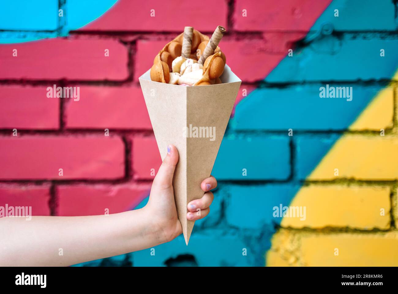 Street food dessert Belgian waffles in hand on a colored wall ...