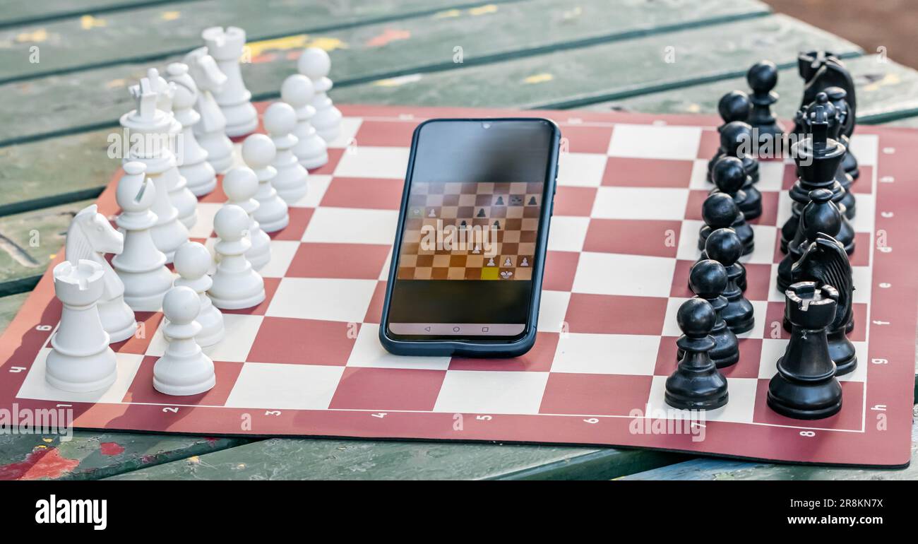 A chess app on a smartphone and a real chessboard with pieces on a ...