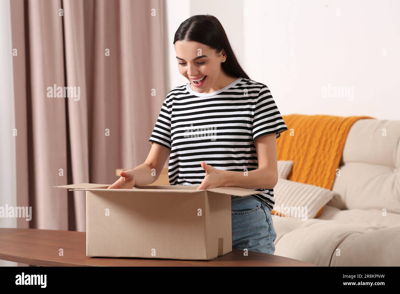 Emotional young woman opening parcel at home. Internet shopping Stock ...