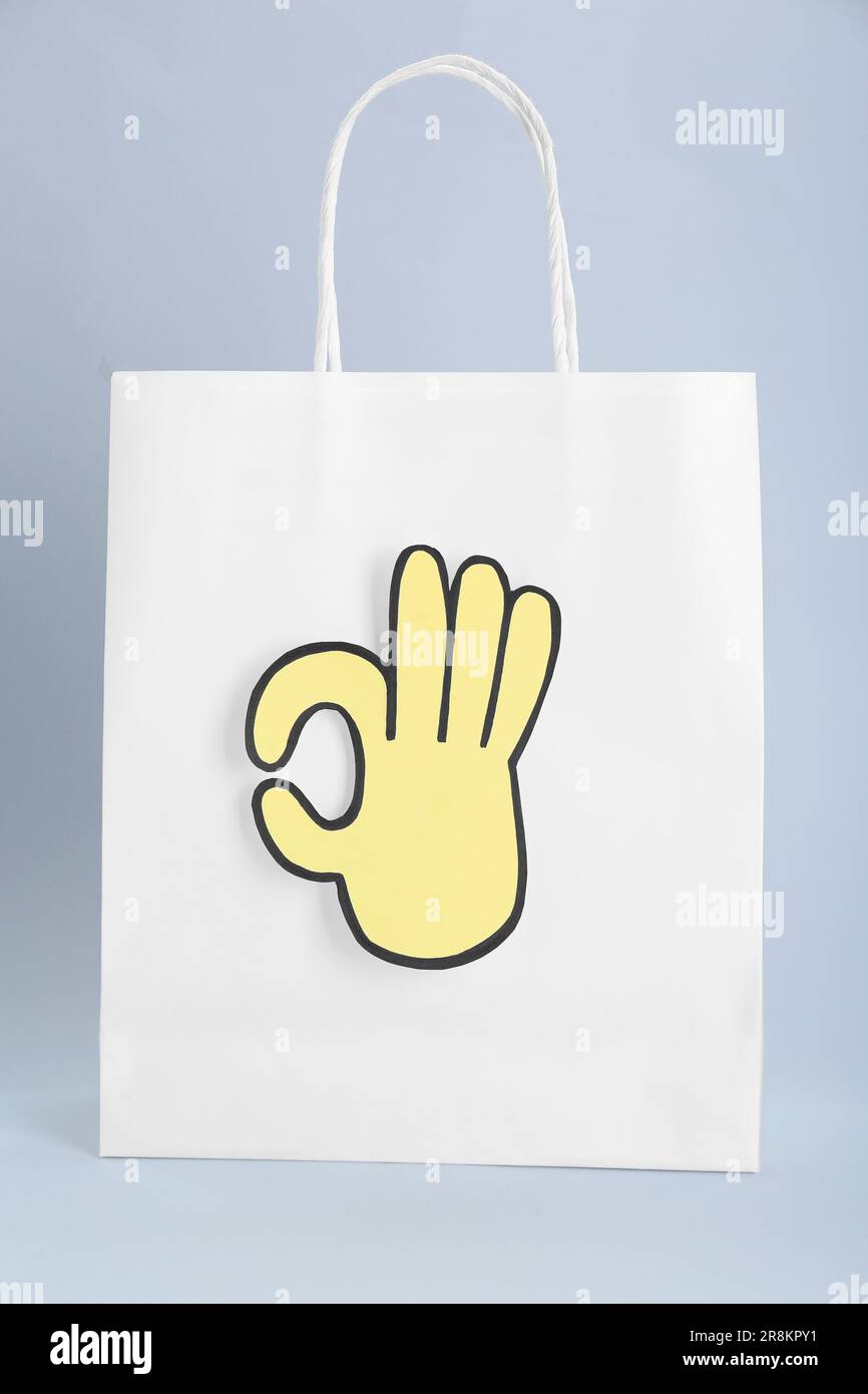 Paper bag and cutout of okay hand gesture on light grey background ...