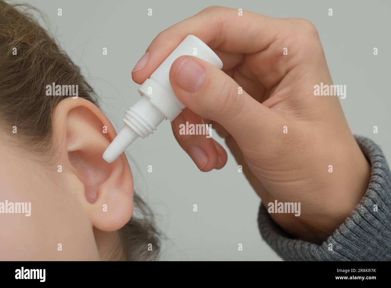 Mother dripping medication into daughter's ear on light grey background ...