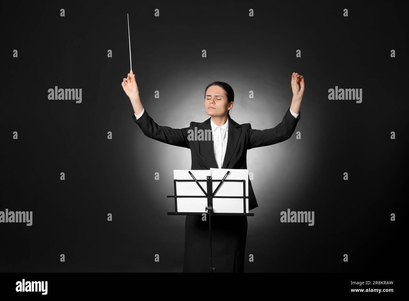 Professional conductor with baton and note stand on black background ...