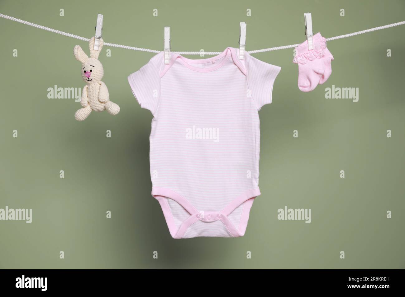Cute small baby clothes and toy hanging on washing line against green ...