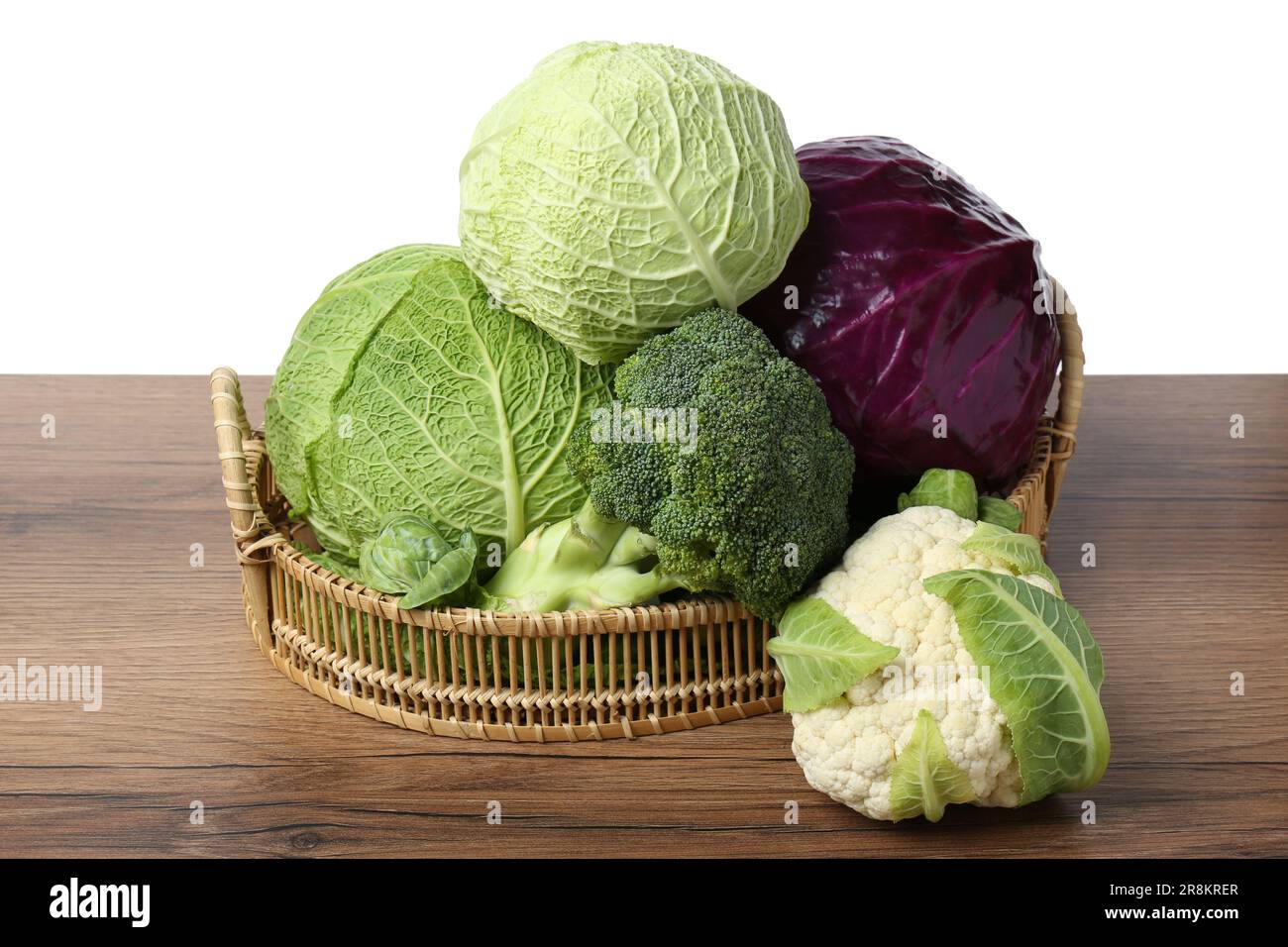 Wicker tray with different types of fresh cabbage on wooden table ...