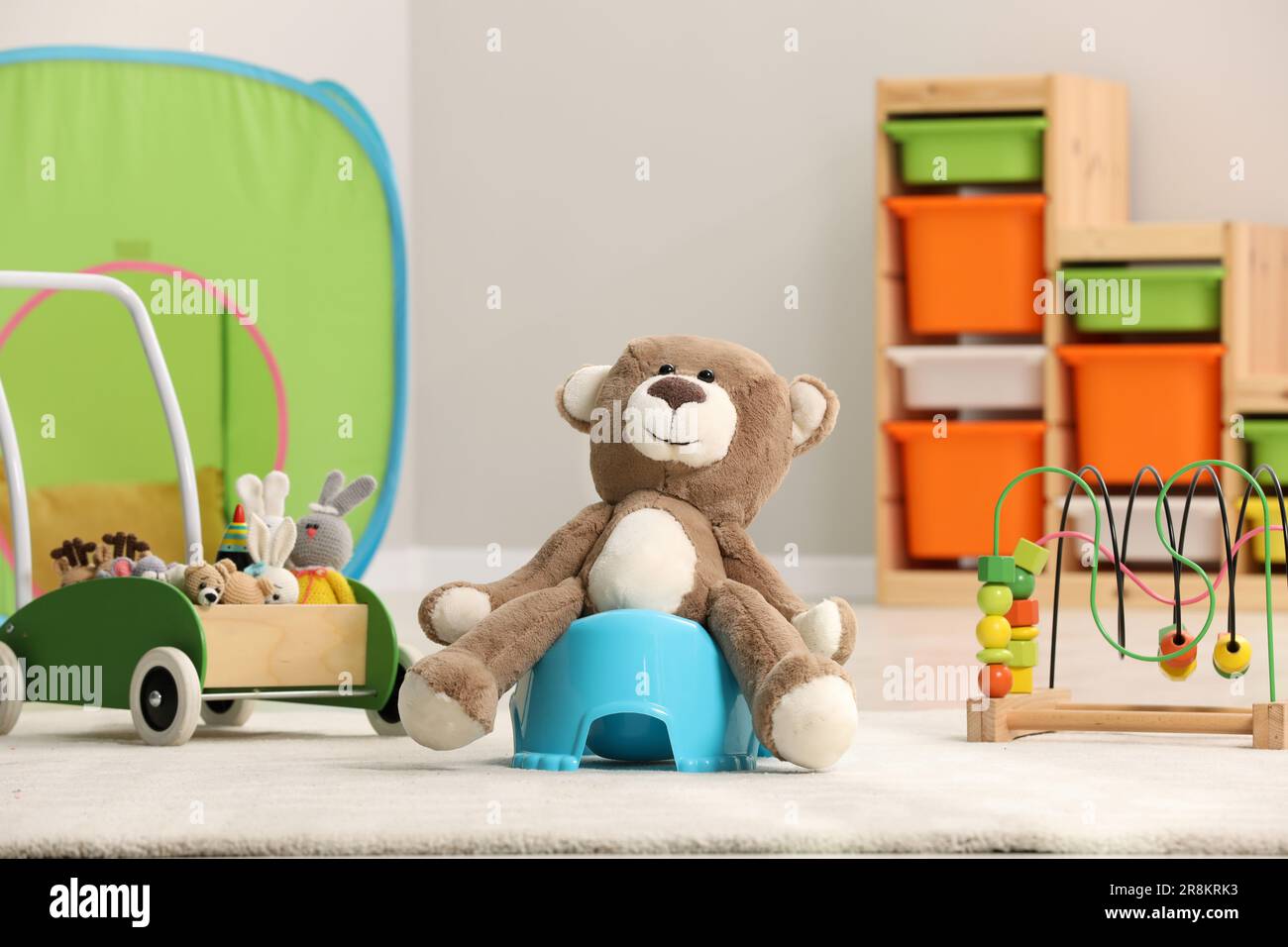 Cute teddy bear on light blue baby potty on floor in room. Toilet ...