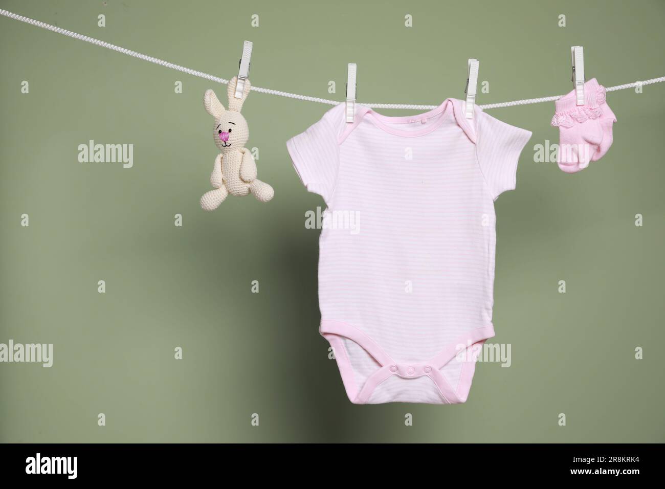 Cute small baby clothes and toy hanging on washing line against green ...