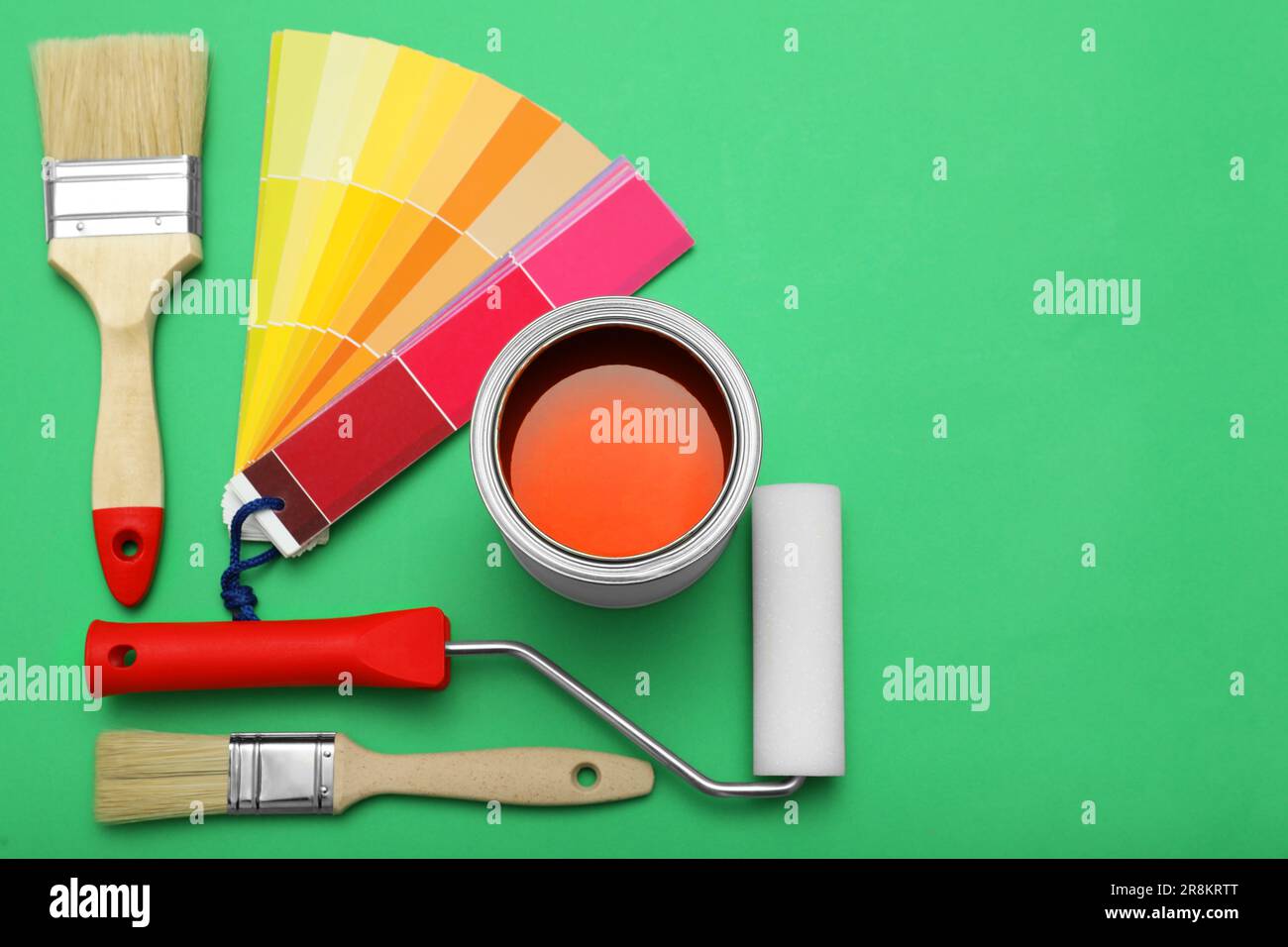 Can of orange paint, roller, brushes and color palette samples on green ...