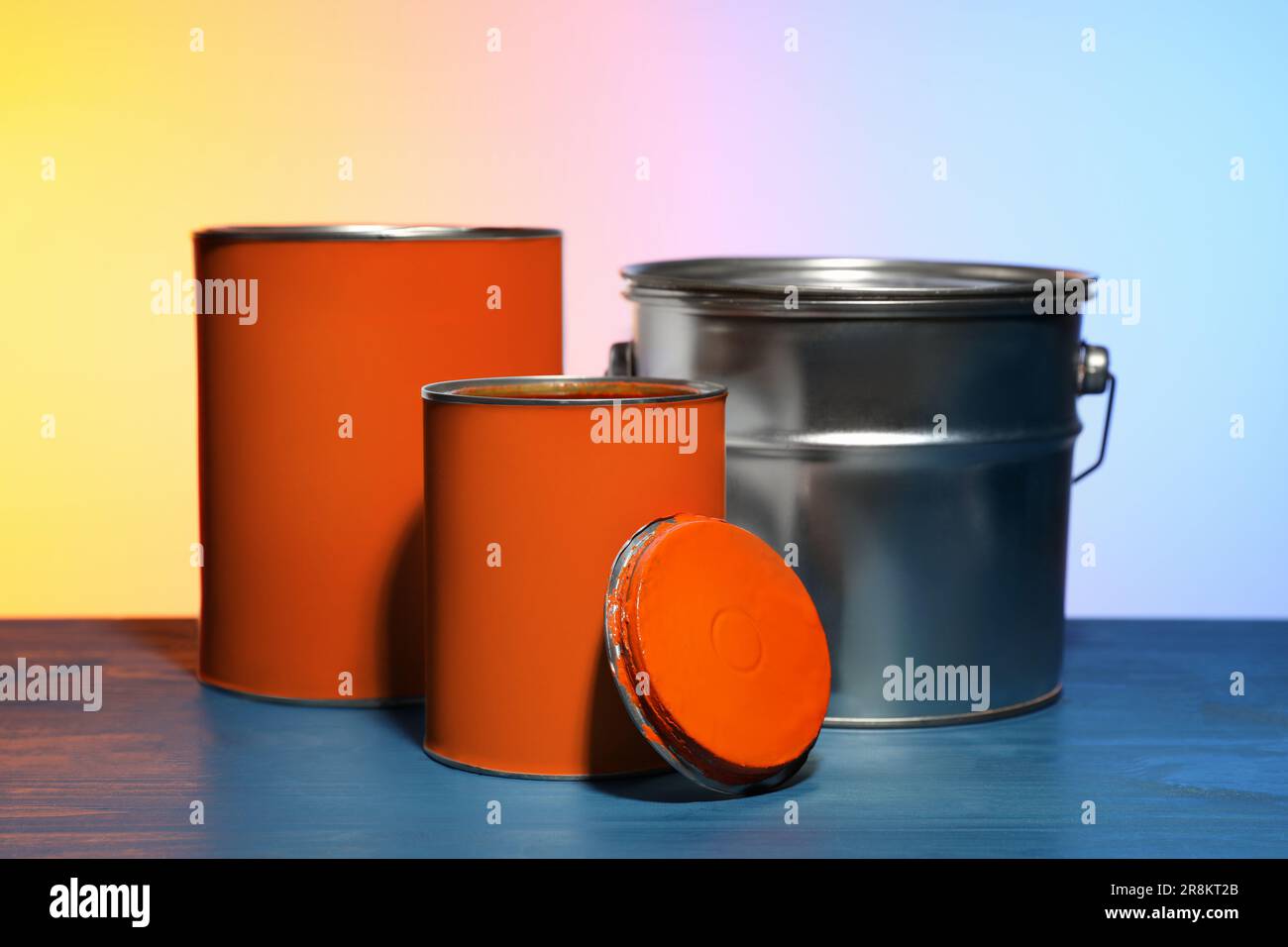 Cans and bucket of orange paint on wooden table against color ...