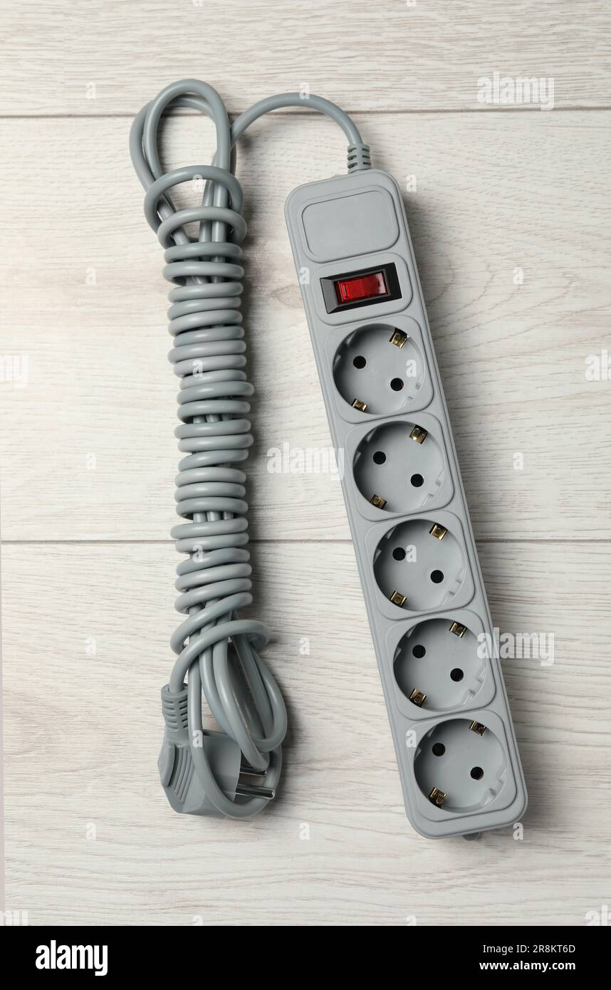 Power strip with extension cord on white wooden floor, top view ...