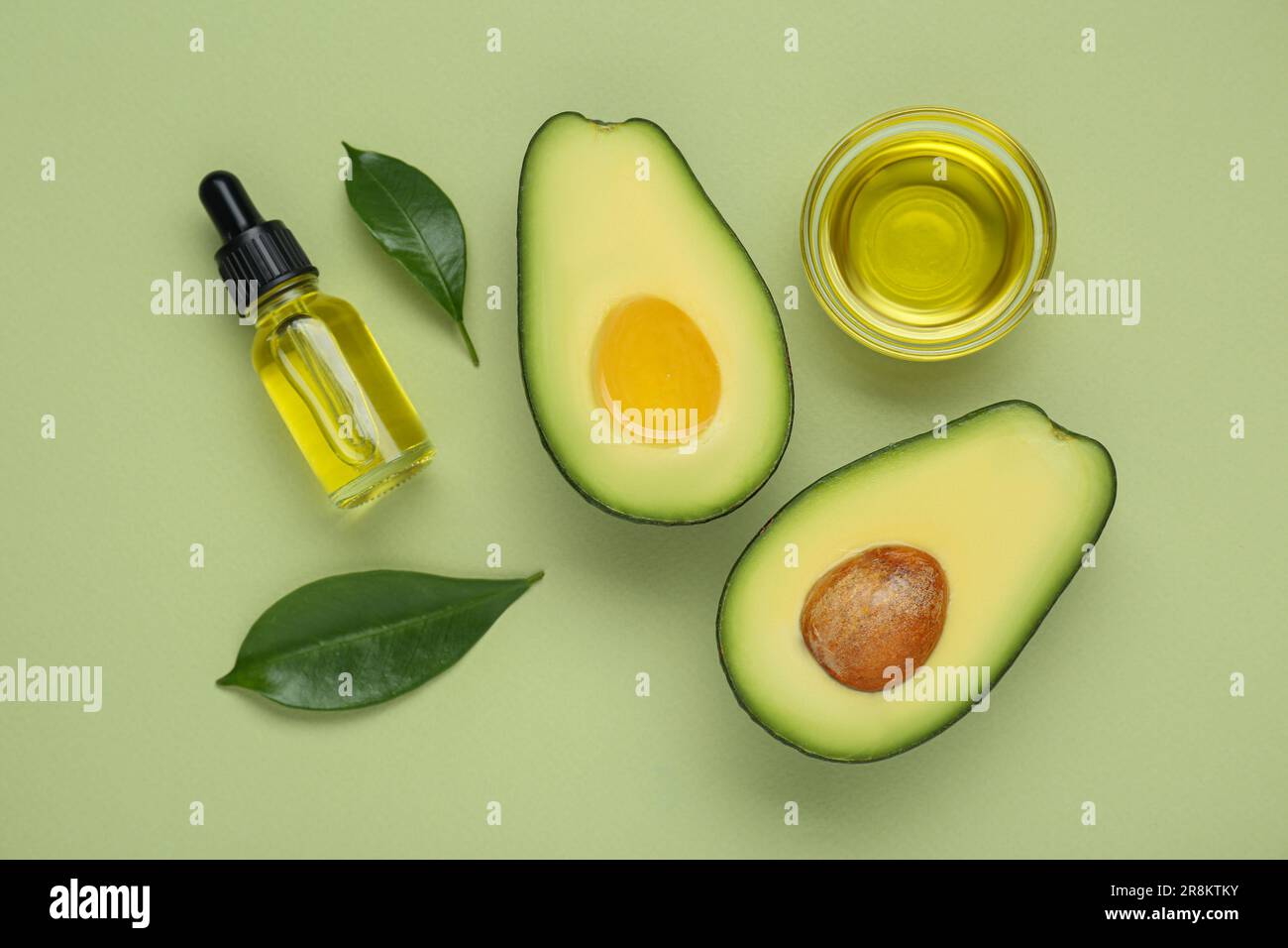 Essential oil, fresh cut avocados and leaves on light green background ...