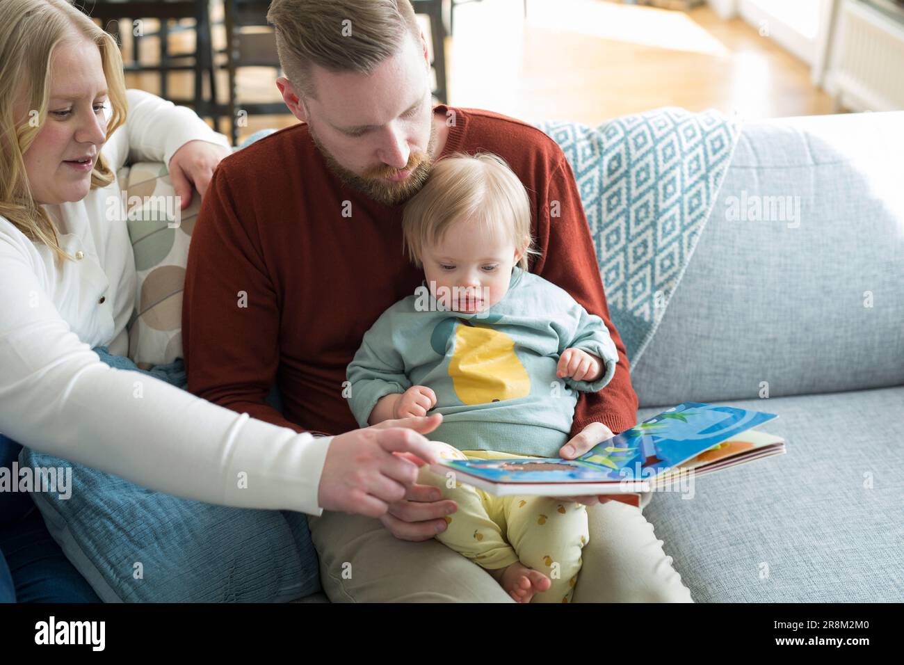 Parents with baby with down syndrome reading a book Stock Photo - Alamy