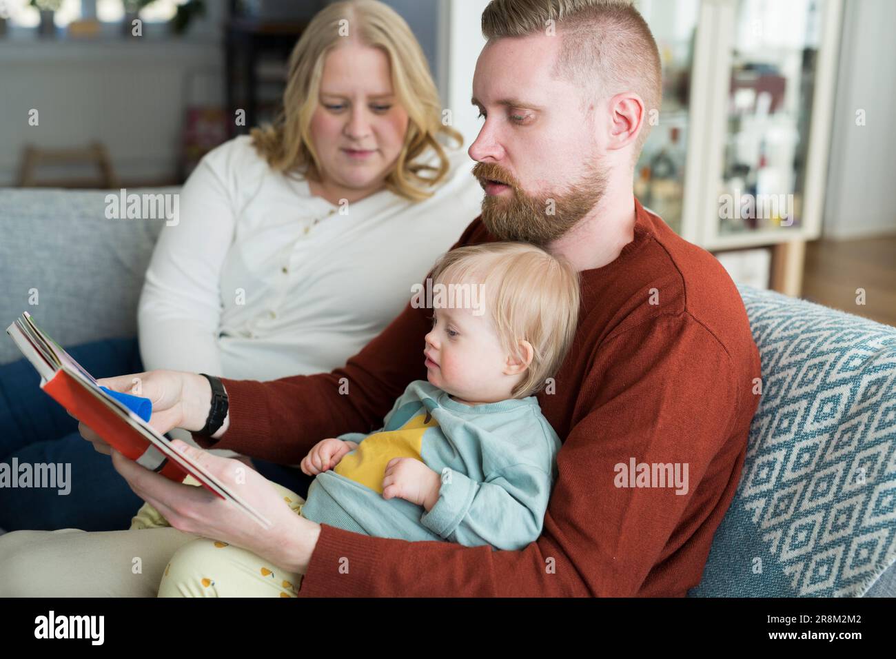 Parents with baby with down syndrome reading on sofa Stock Photo - Alamy