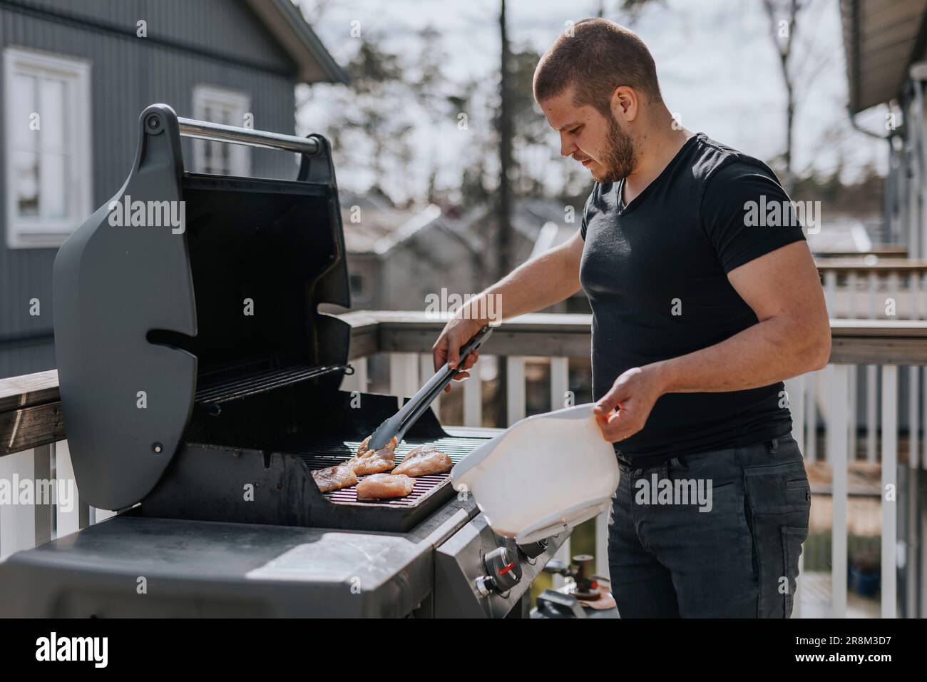 Man on balcony grilling chicken Stock Photo - Alamy