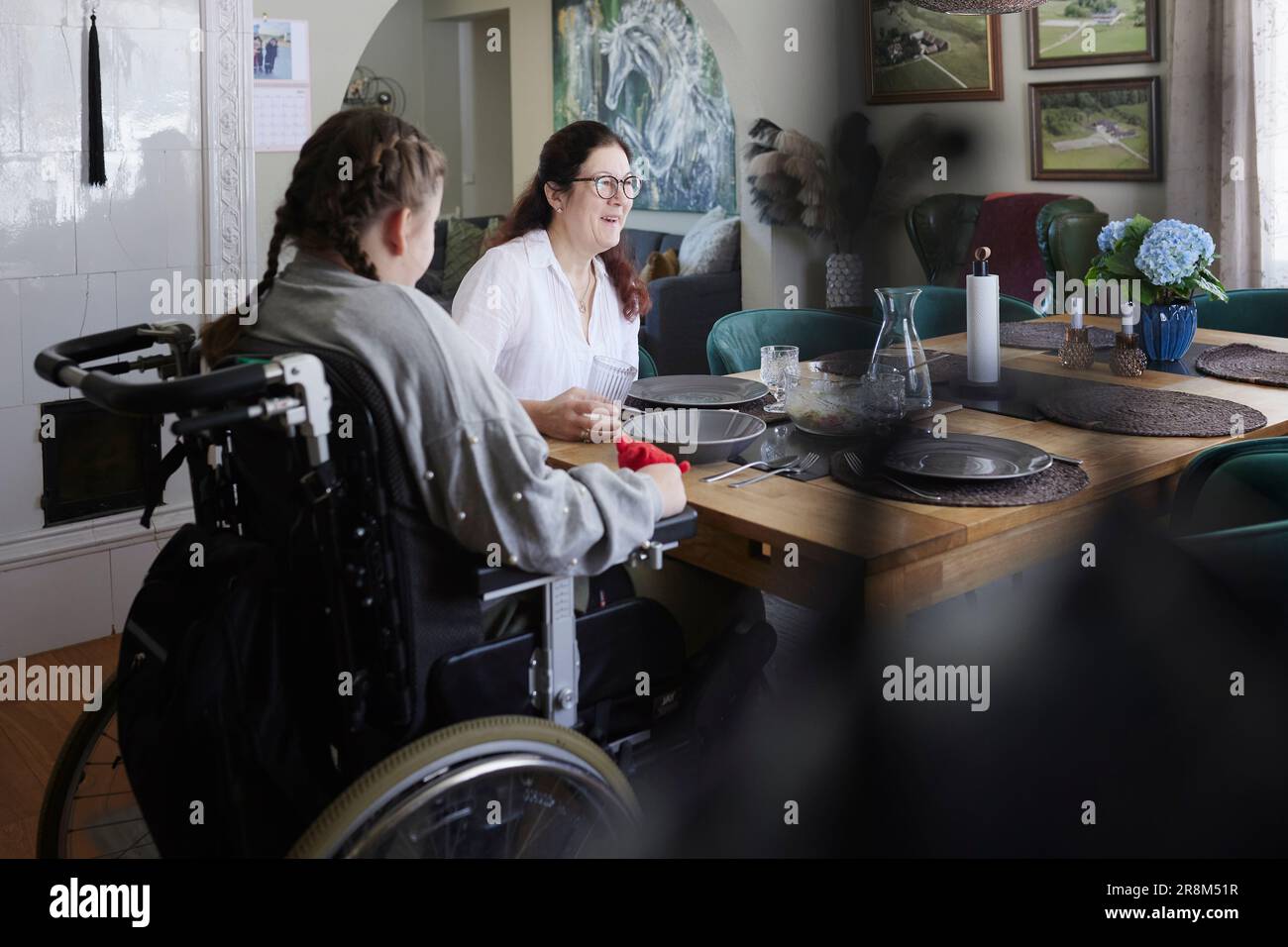 Mother and disabled teenage daughter in wheelchair sitting at kitchen ...