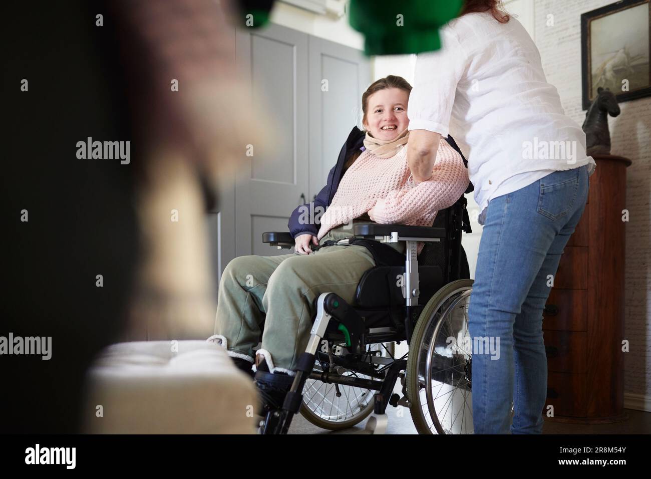 Mother helping disabled daughter in wheelchair putting coat on Stock ...