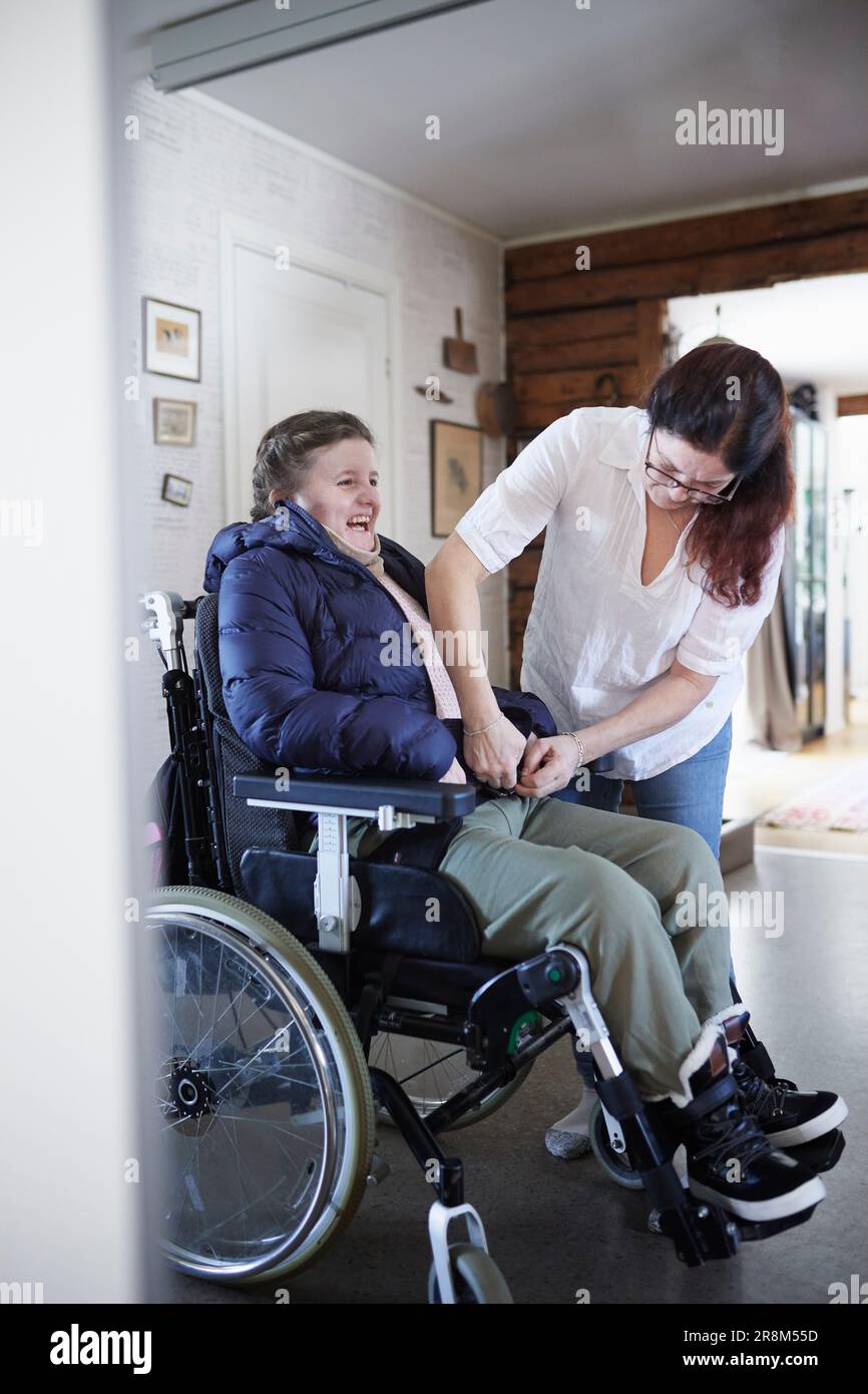 Mother helping disabled daughter in wheelchair putting coat on Stock ...