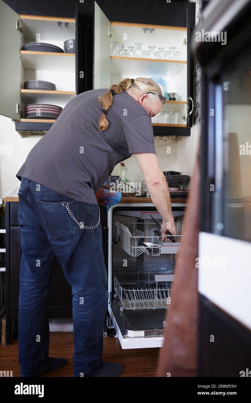 Man in kitchen taking dishes out of dishwasher Stock Photo - Alamy