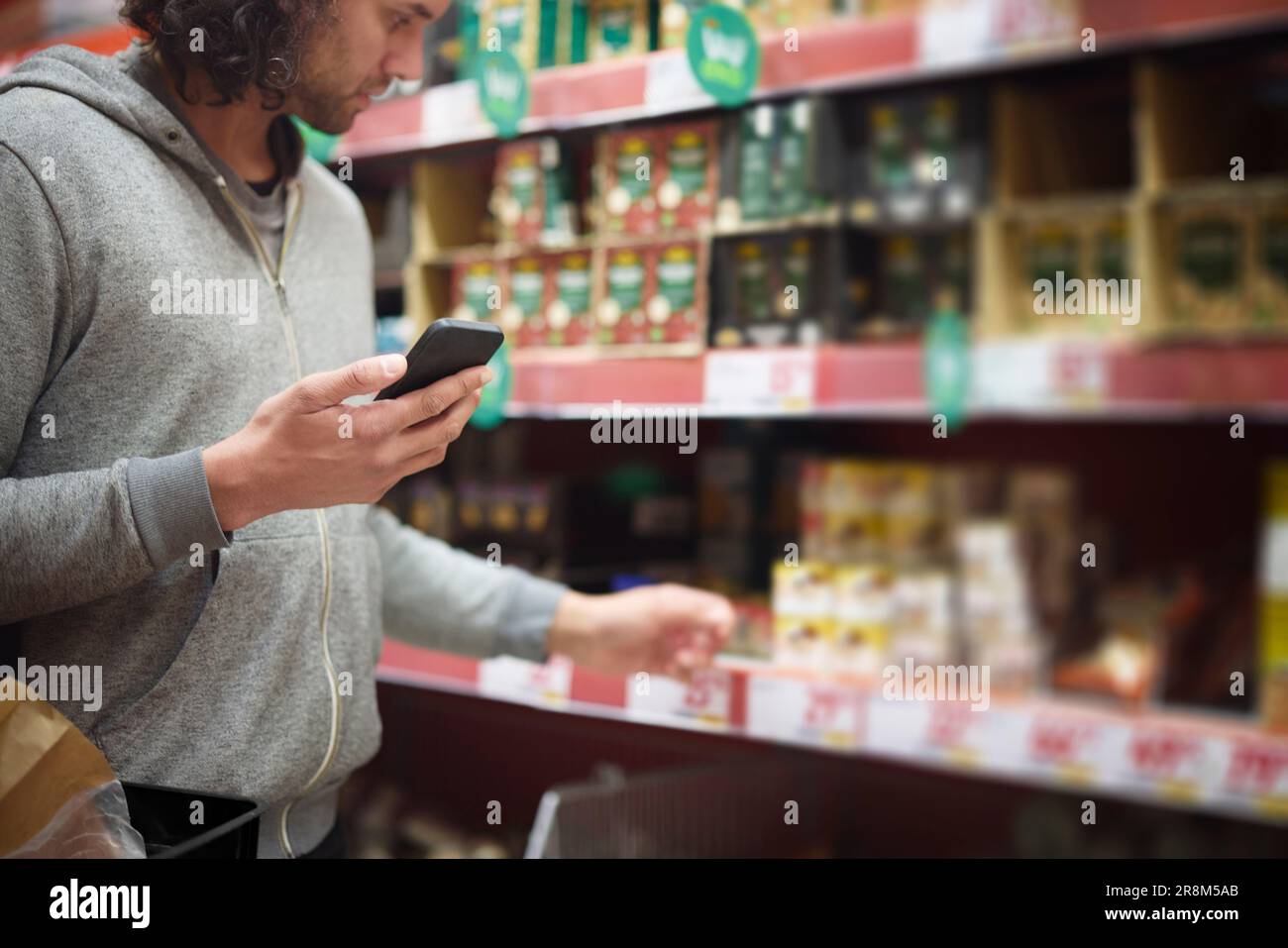 Man in supermarket comparing prices during inflation on cell phone ...