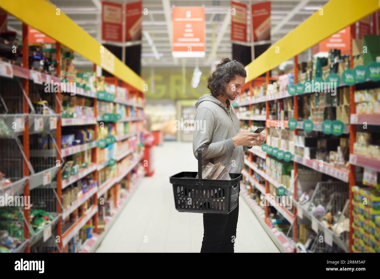 Man in supermarket comparing prices during inflation on cell phone ...