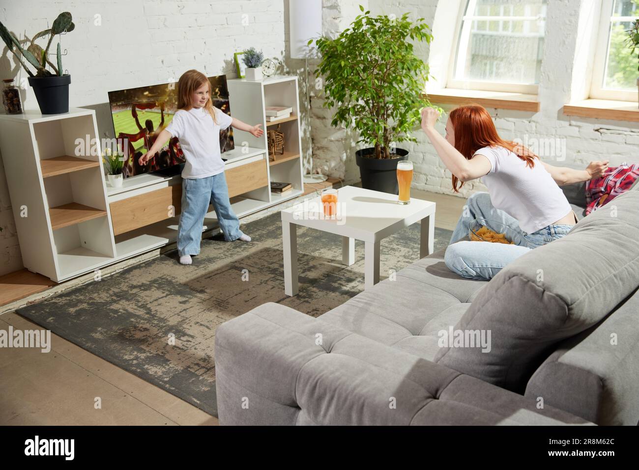 Young woman sitting on couch at home and watching football match on tv ...