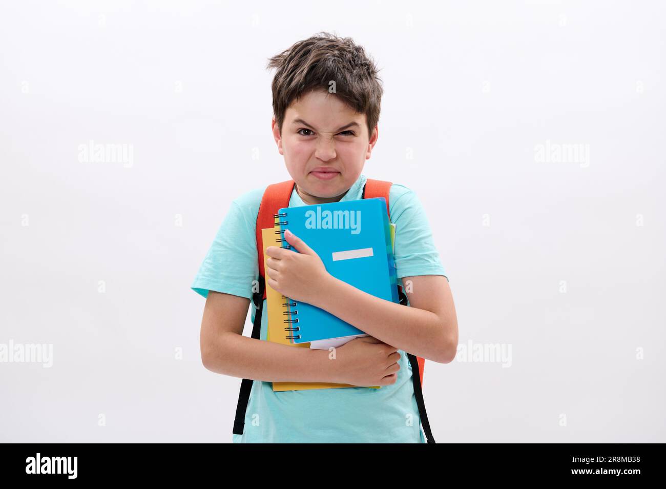 Irritated angry schoolboy holding workbooks, expresses negative ...