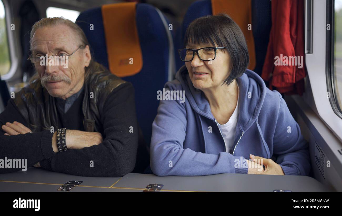 Elderly couple is riding in a train carriage and talking with each ...