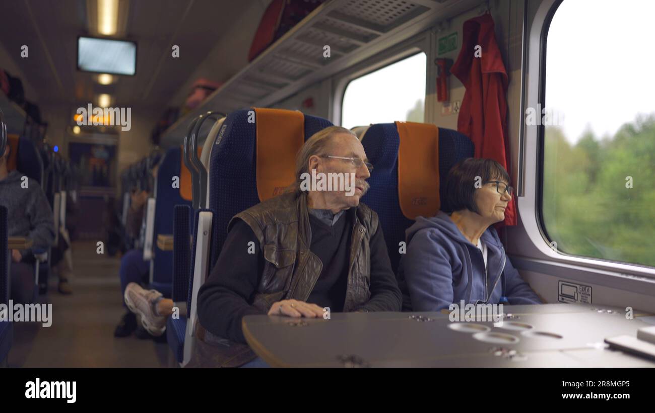 Elderly couple is riding in a train carriage and looking out the window ...
