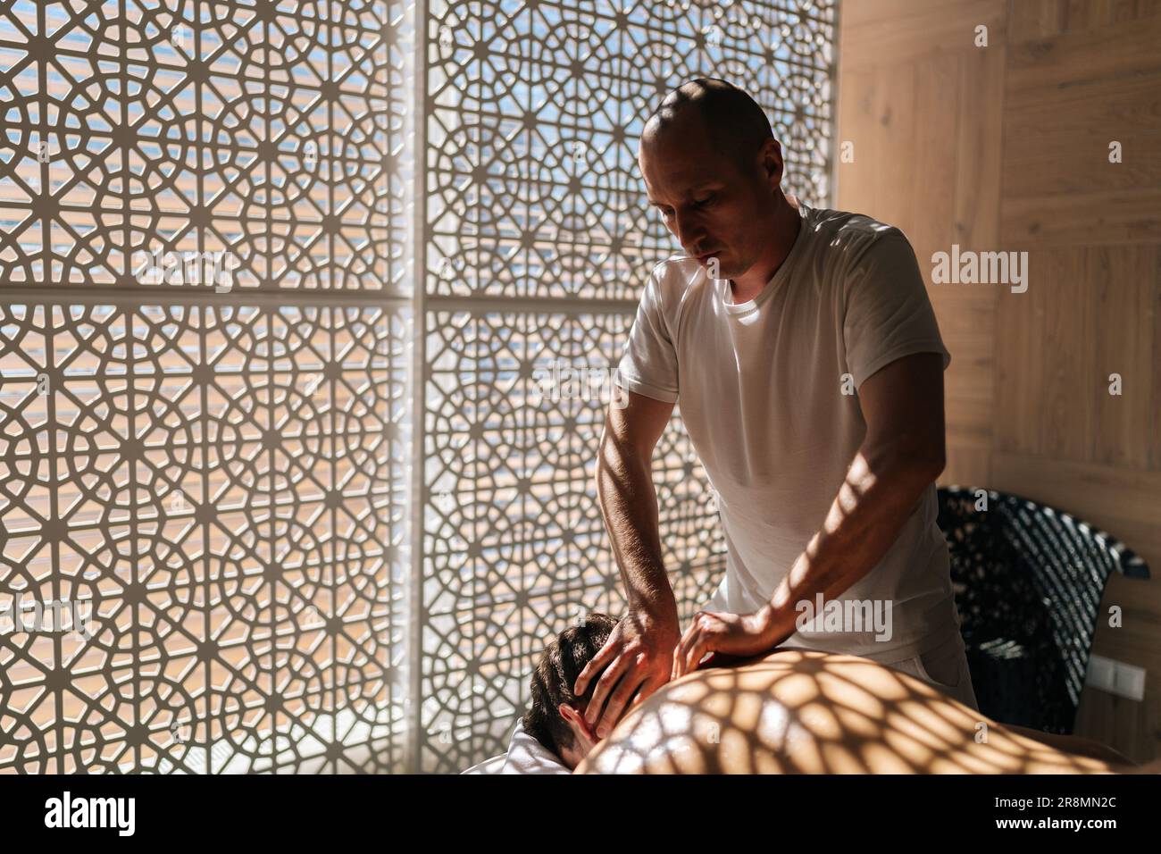 Side view of concentrated male masseur massaging neck of young sporty man lying on massage table ...