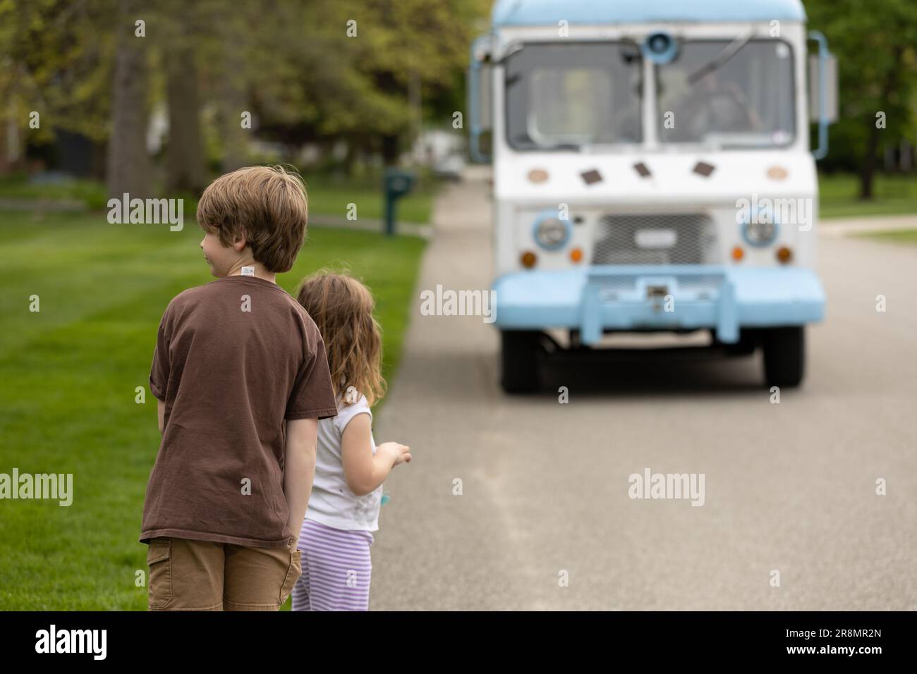 A Brother And Sister Wait Patiently As The Ice Cream Man Drives His Ice