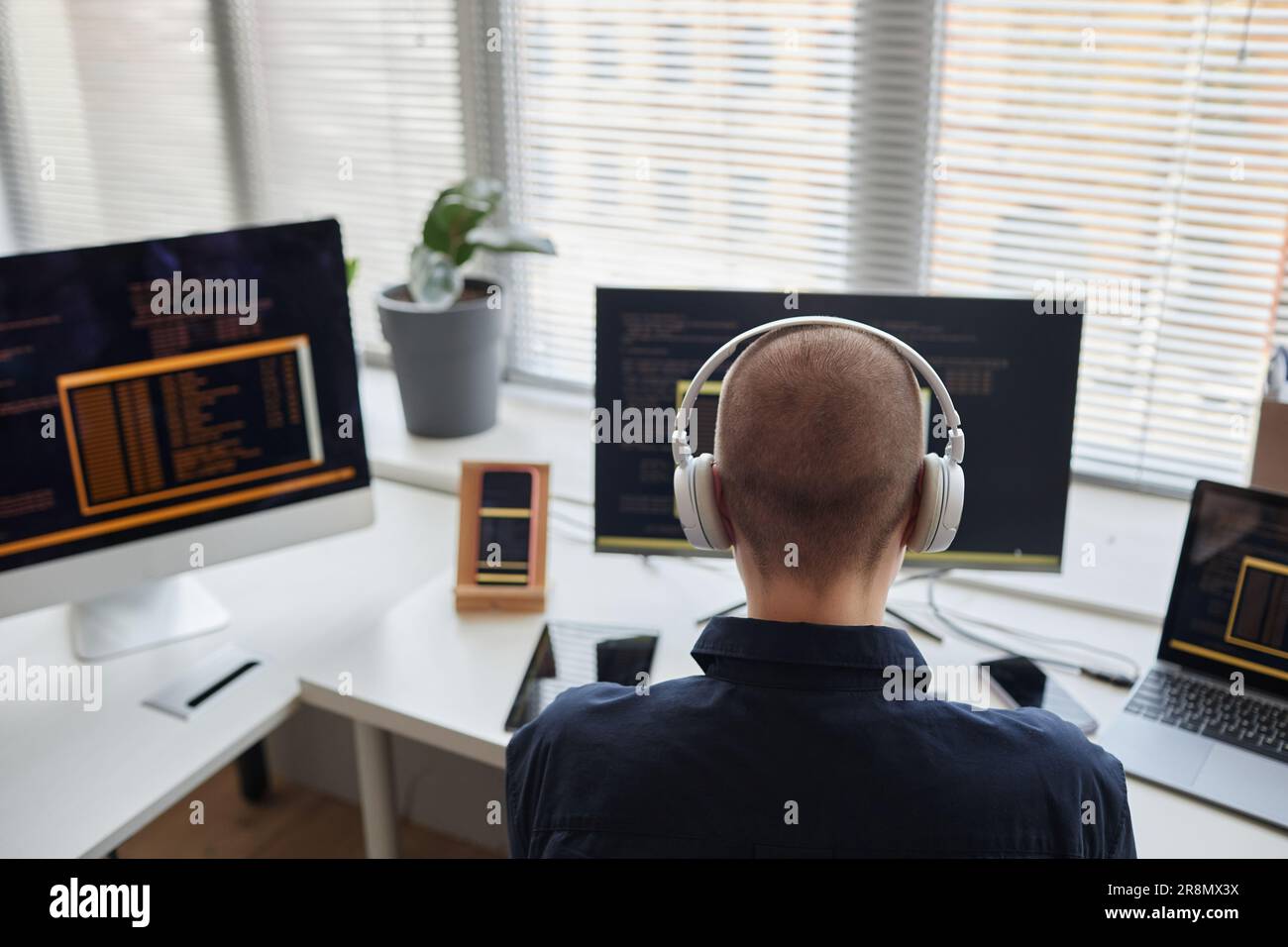 Back view of bald young woman as female programmer wearing headphones ...