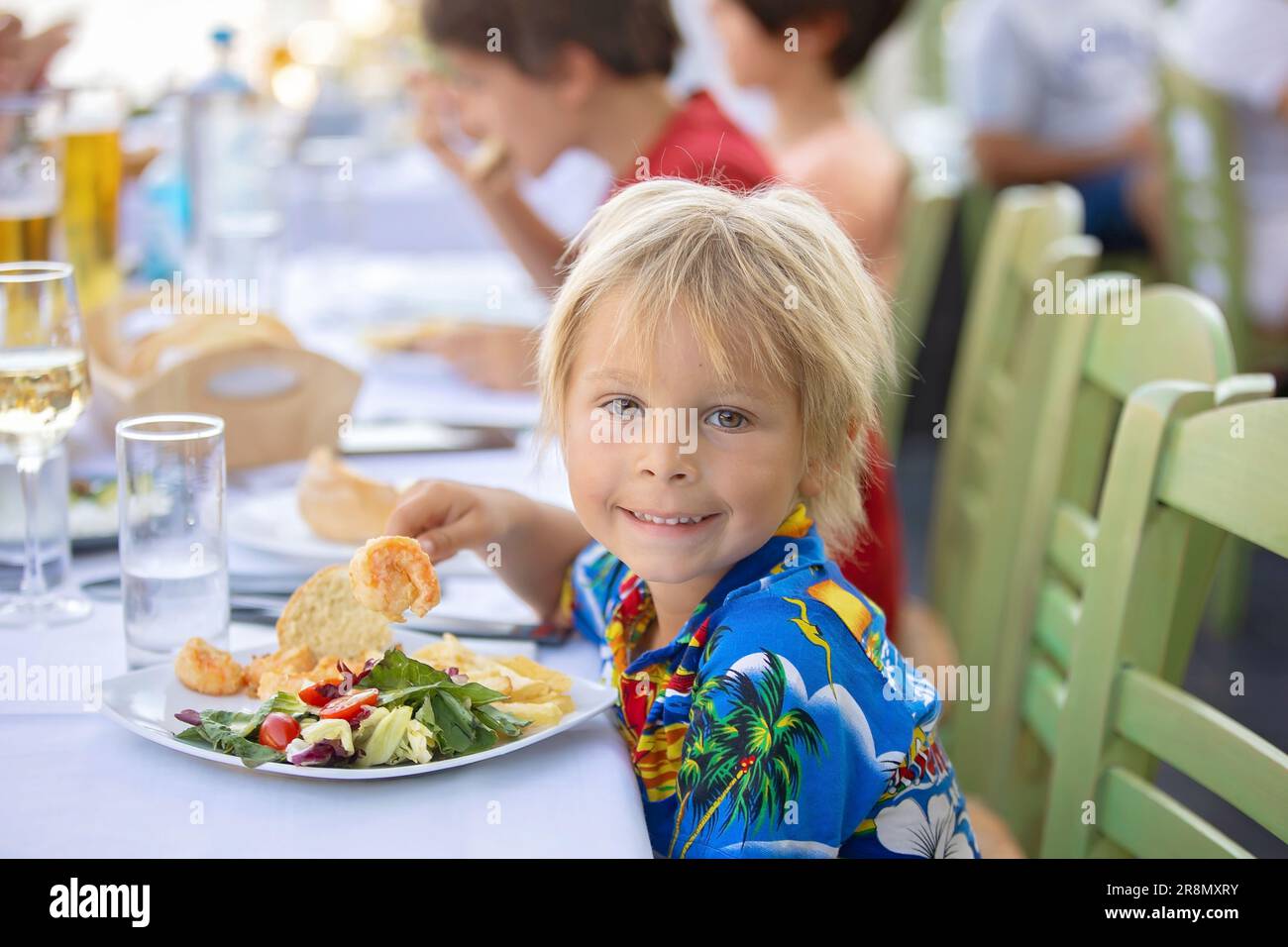 Sweet child, sitting in restaurant summertime outdoor, eating seafood ...