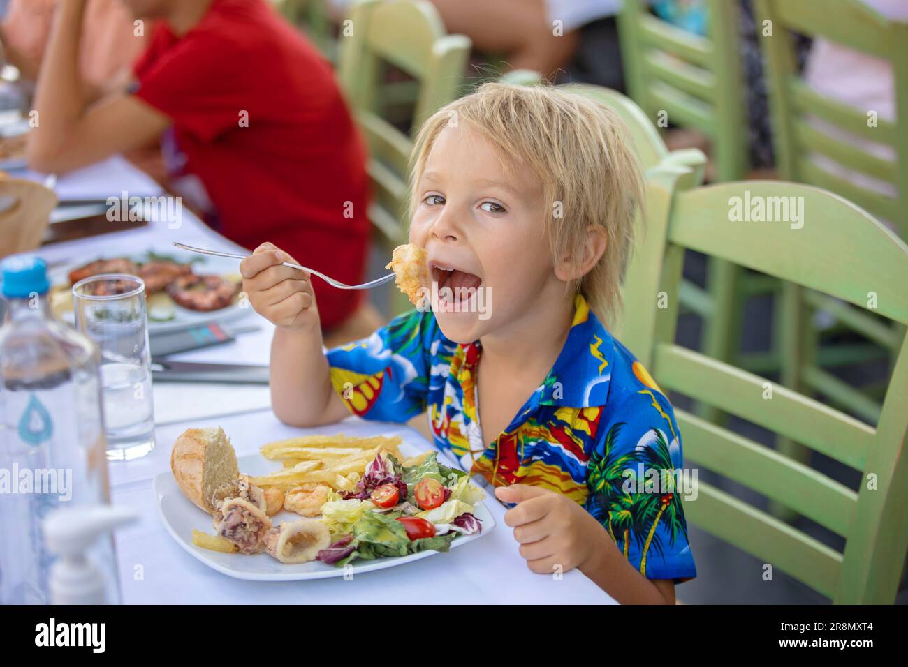 Sweet child, sitting in restaurant summertime outdoor, eating seafood ...