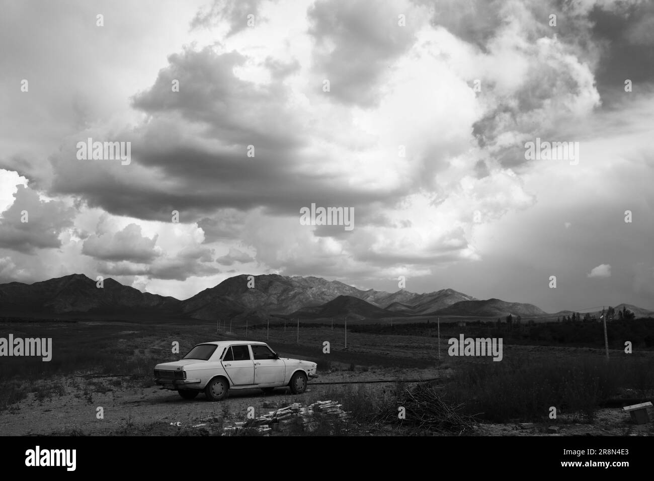 A grayscale shot of an old abanoned car parked in a vast desert ...