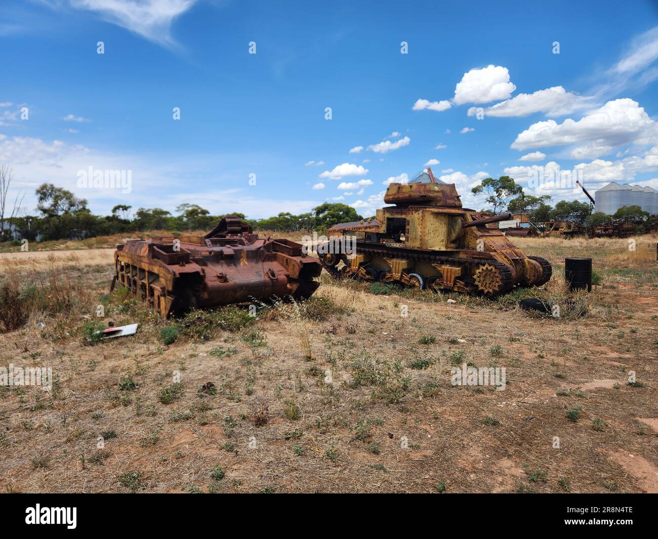A close-up view of two vintage, rusty tanks situated on a dirt ground ...