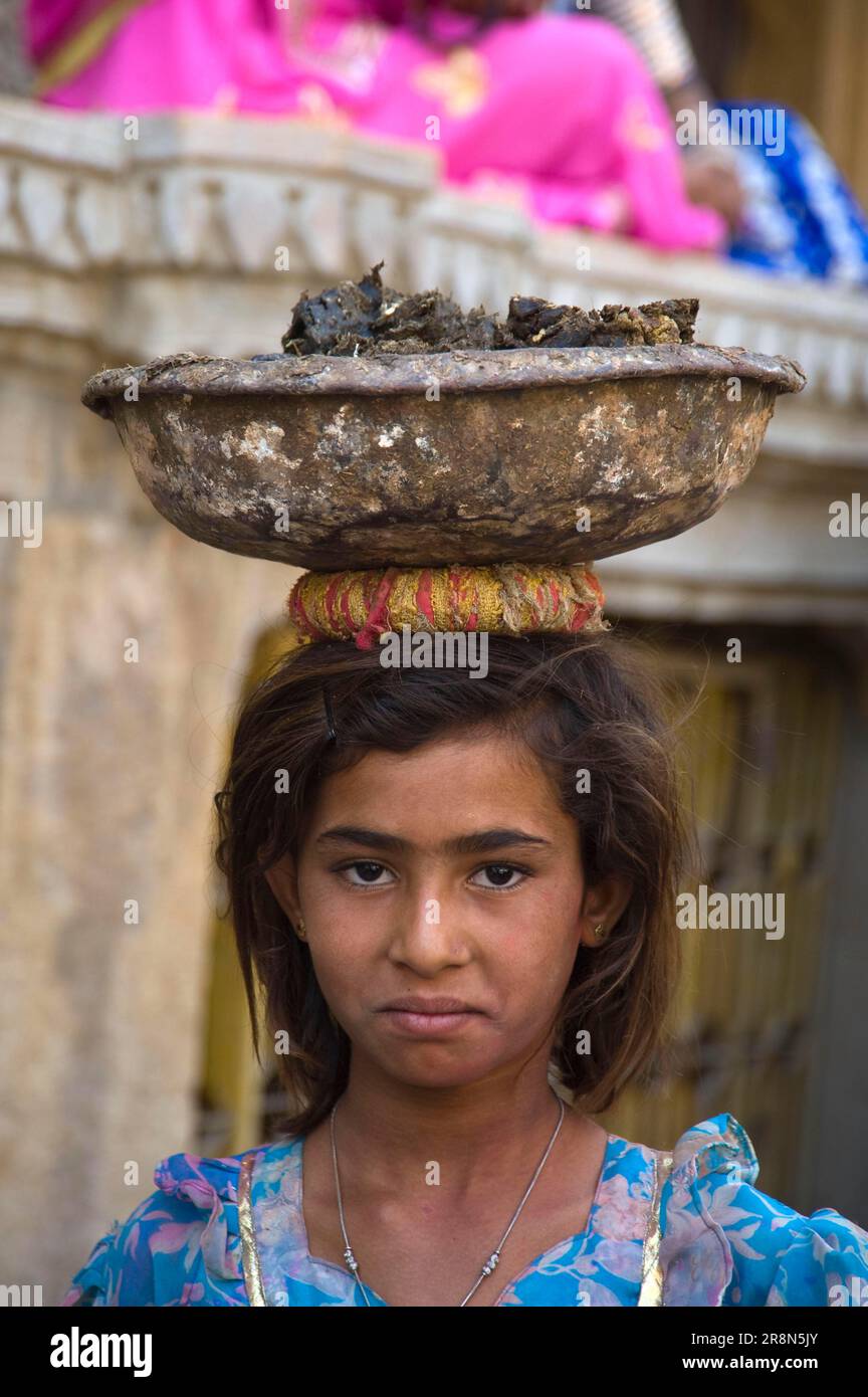 Indian girl carrying basin with cow dung on her head, Jaisalmer ...