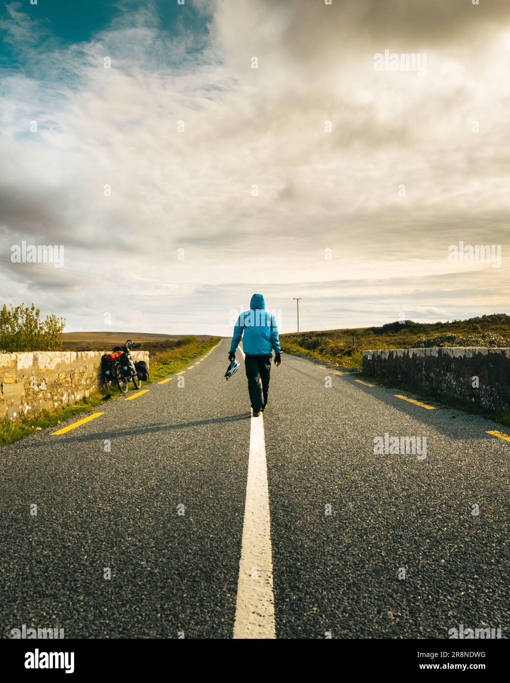 Back view male cyclist in blue jacket walk on road by touring bicycle ...