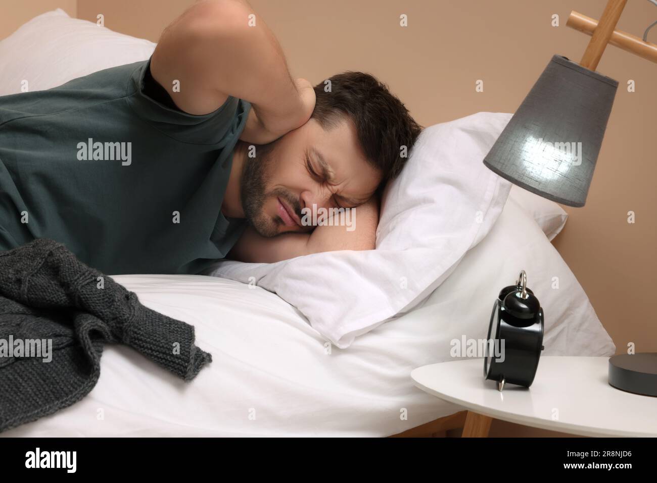 Sleepy man covering his ears with hands in bed at home Stock Photo - Alamy
