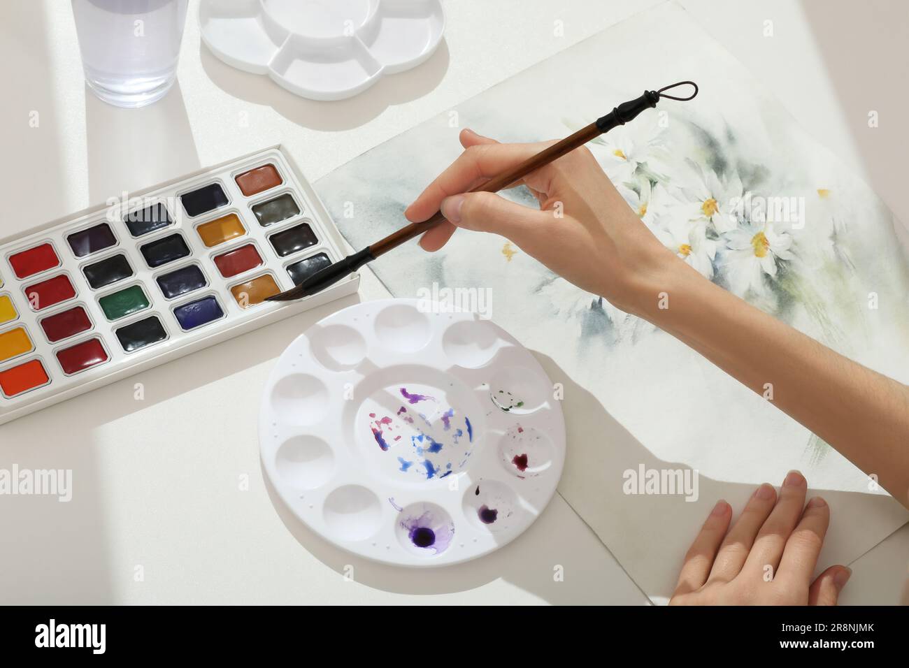 Woman painting flowers with watercolor at white table, above view ...