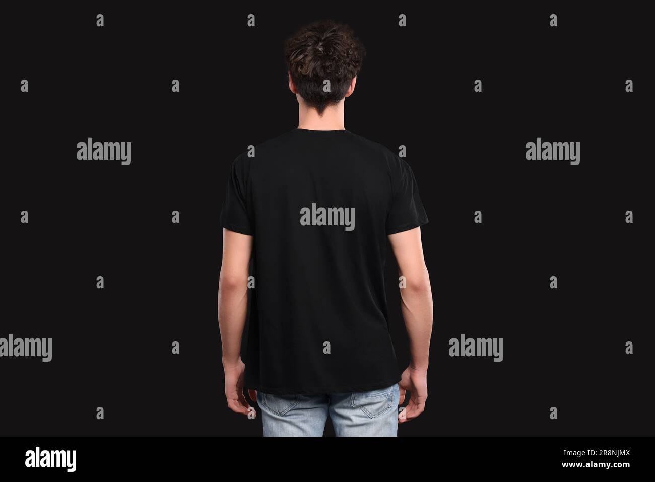Man wearing stylish t-shirt on black background, back view. Mockup for ...